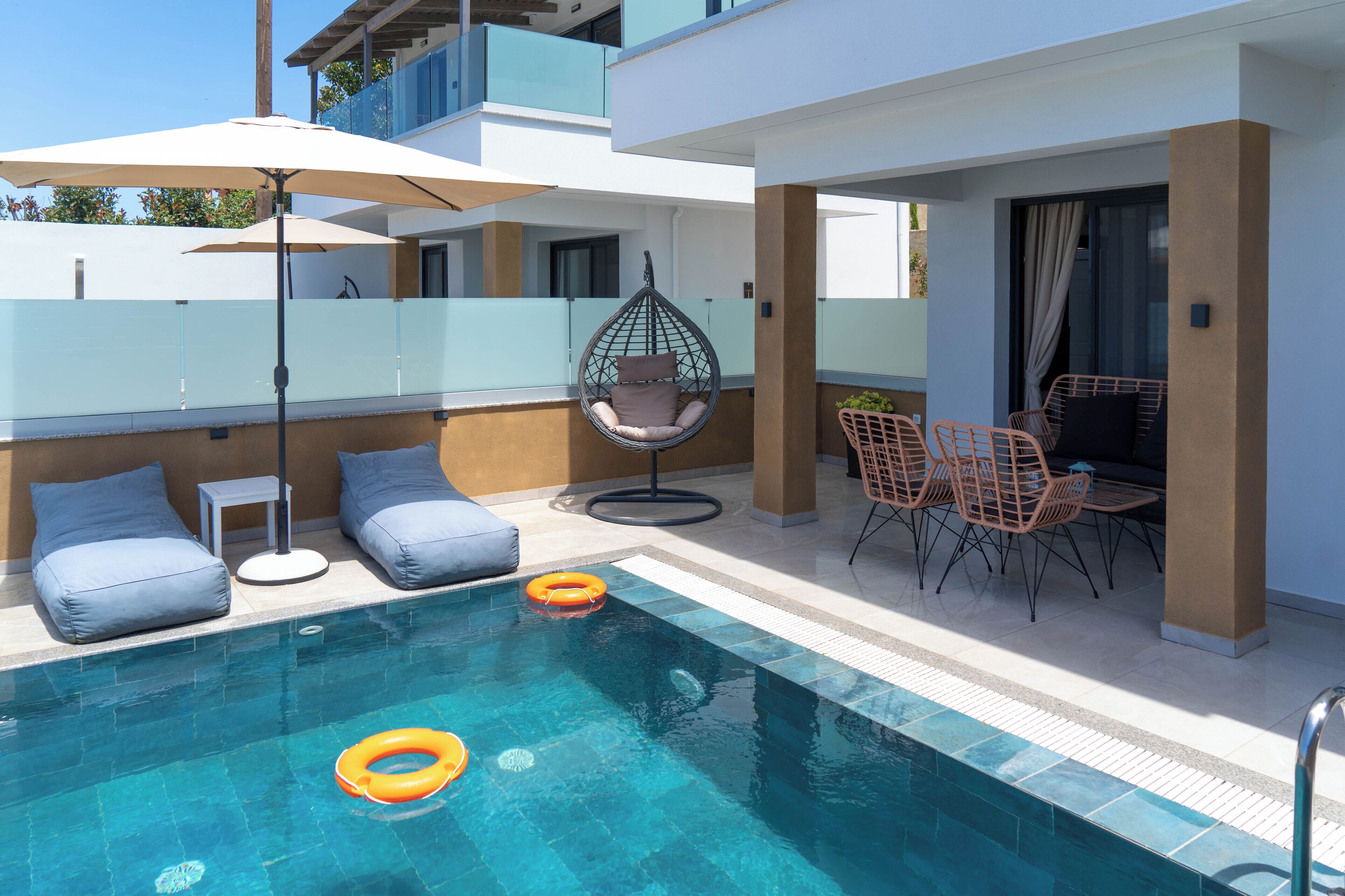 Uma área de piscina moderna ao ar livre, com uma cadeira suspensa, espreguiçadeiras e uma mesa.