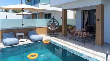 Uma área de piscina moderna ao ar livre, com uma cadeira suspensa, espreguiçadeiras e uma mesa.