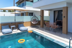 Uma área de piscina moderna ao ar livre, com uma cadeira suspensa, espreguiçadeiras e uma mesa.