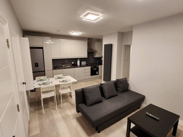 Um apartamento moderno com área de jantar, cozinha compacta e sala de estar com sofá e mesa de centro.