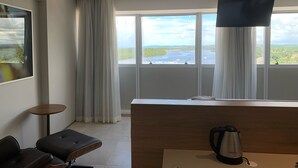 Quarto de hotel moderno com uma janela grande, televisão de tela plana, máquina de café e uma pequena mesa redonda.