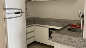 Uma cozinha moderna com armários brancos, micro-ondas embutido, pia de aço inoxidável e bancada de granito.