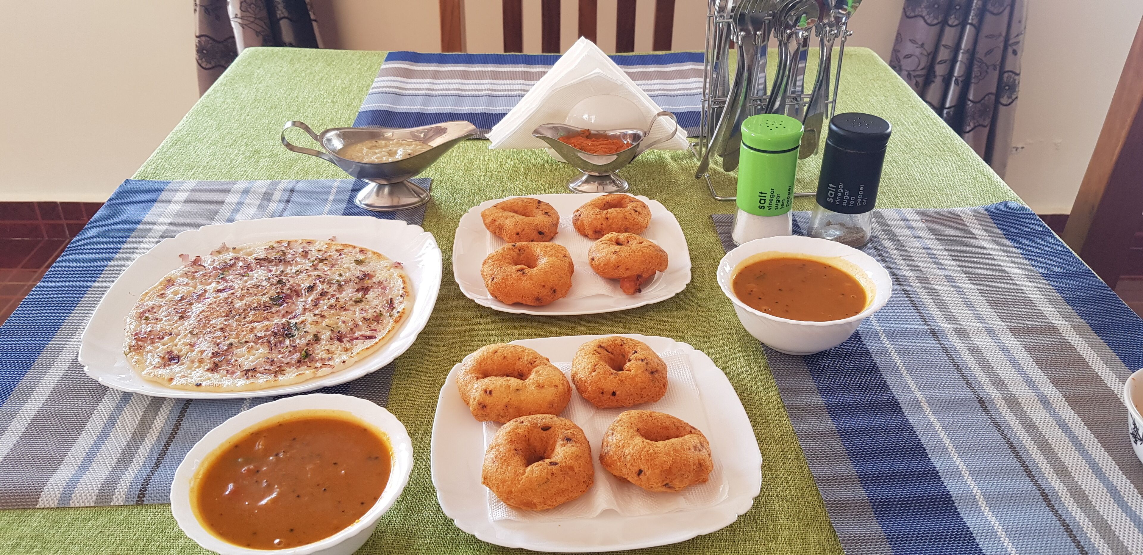 Uma mesa posta com diversos pratos, incluindo um prato de pães achatados, uma tigela de sopa e vários petiscos fritos.