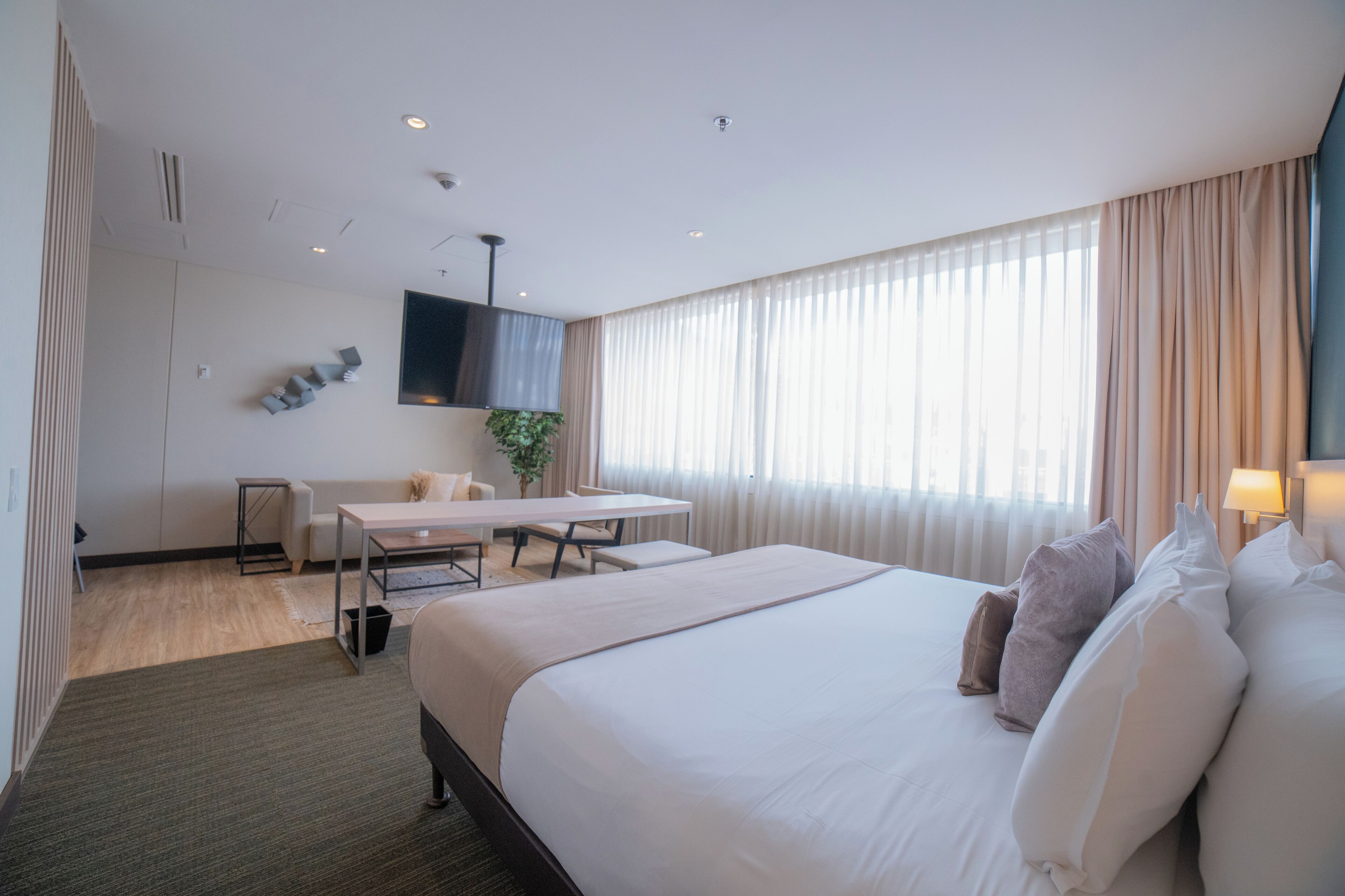 Quarto de hotel moderno com uma cama grande, uma escrivaninha e uma TV fixada na parede.