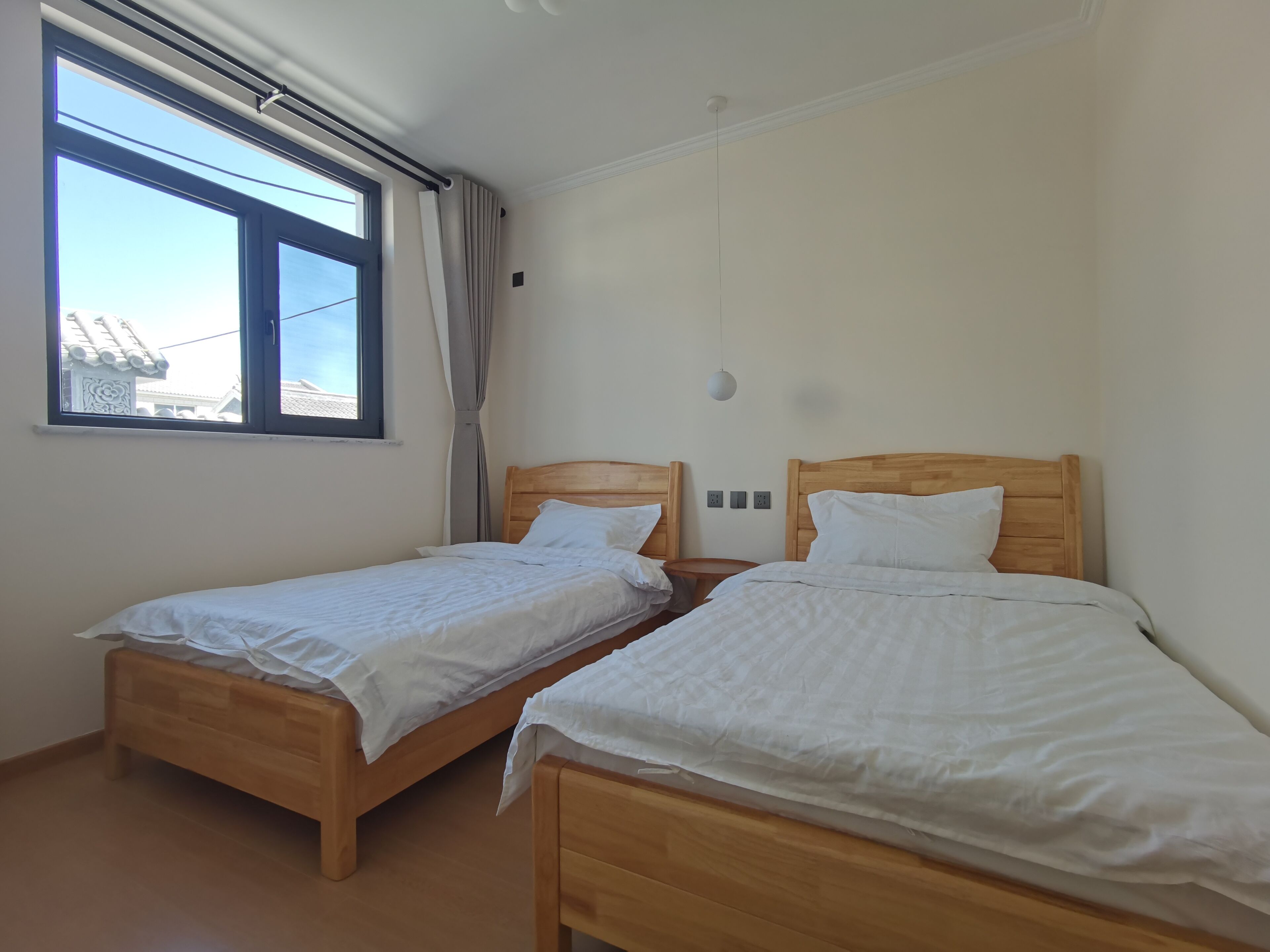 Quarto com duas camas de madeira, uma janela com cortinas e um ponto de luz.