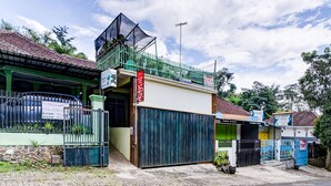 Um edifício de dois andares com varanda verde, portão metálico fechado e uma placa.