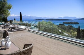 Terraço com vista para um lago e montanhas, mobiliado com cadeiras e uma mesa.