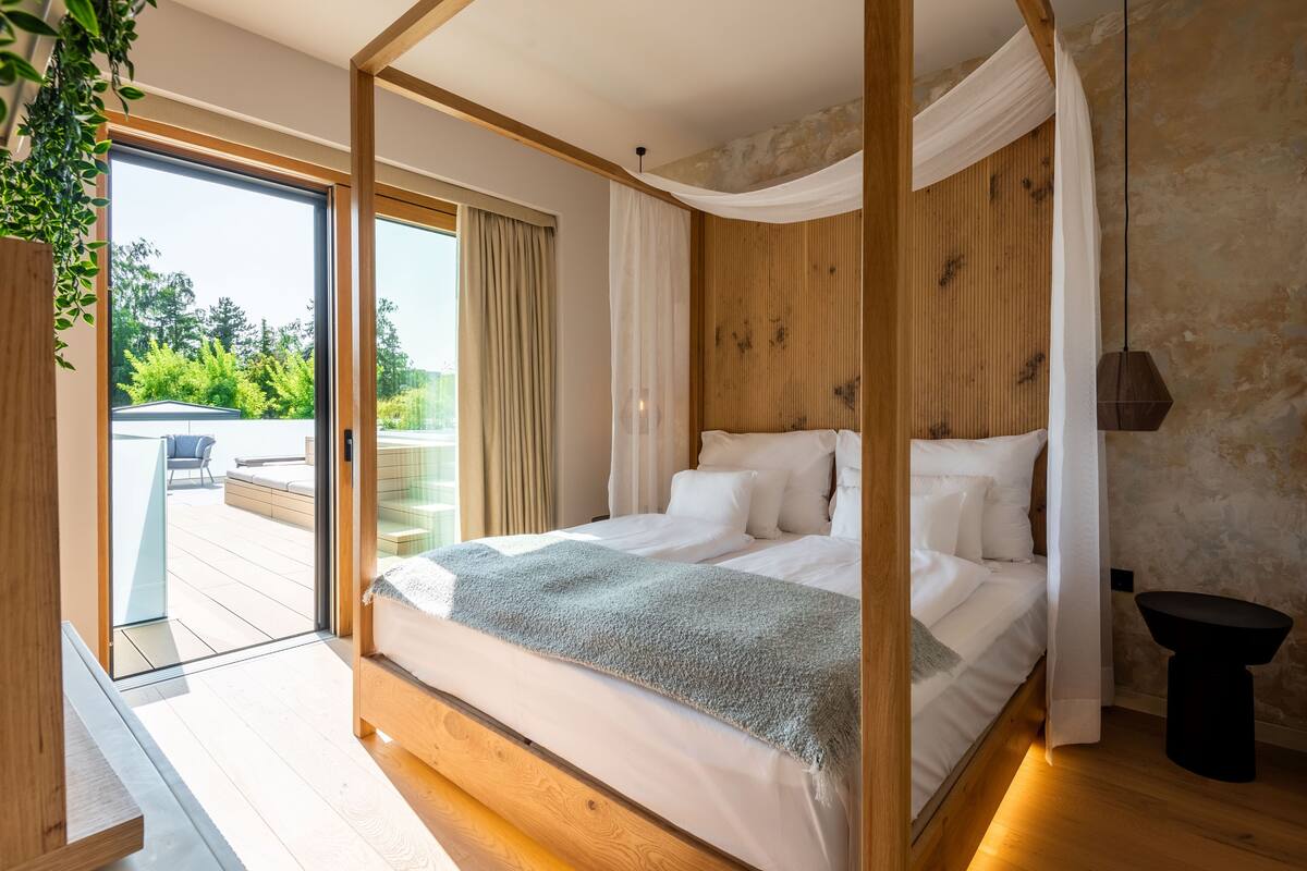 Quarto moderno com cama grande, cabeceira de madeira e vista para uma varanda.