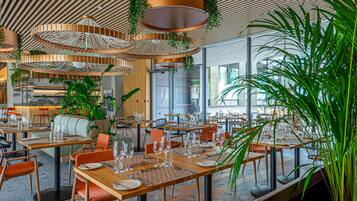 Um restaurante moderno com mesas de madeira, cadeiras laranjas e plantas penduradas.
