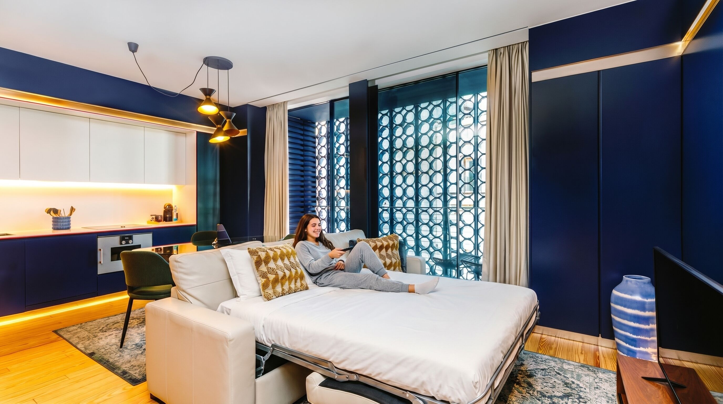 Quarto de hotel moderno com uma cama, uma escrivaninha e uma janela grande com um padrão geométrico.