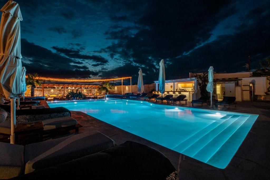 Piscina com espreguiçadeiras e guarda-sóis, rodeada por um edifício com área de bar.