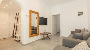 Uma sala de estar com sofá, escada de madeira, espelho e TV de tela plana fixada na parede.