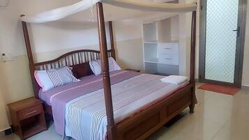 Uma cama de dossel com cortina, mesa de cabeceira, guarda-roupa e porta com painel de vidro.