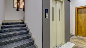 Interior de hotel com escadaria de mármore, elevador e porta de madeira.