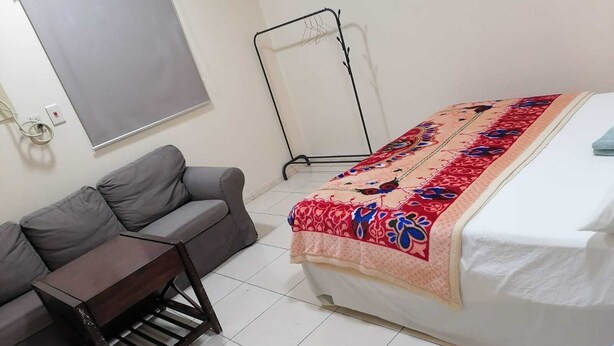 Um quarto com uma cama, um sofá cinza, uma mesinha de madeira e um ventilador.
