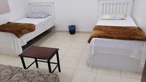 Quarto pequeno e limpo com duas camas de solteiro, uma mesinha e um sofá estampado.