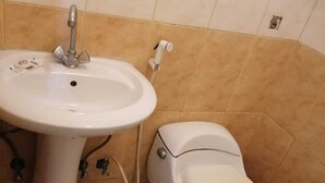 Um banheiro com pia branca e vaso sanitário, azulejos bege nas paredes e um par de chinelos no chão.