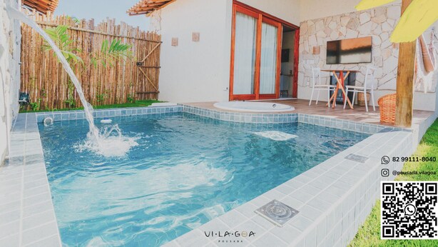 Piscina cercada por um bambuzal, uma parede de pedra e um deck revestido com azulejos, com mobiliário de exterior.