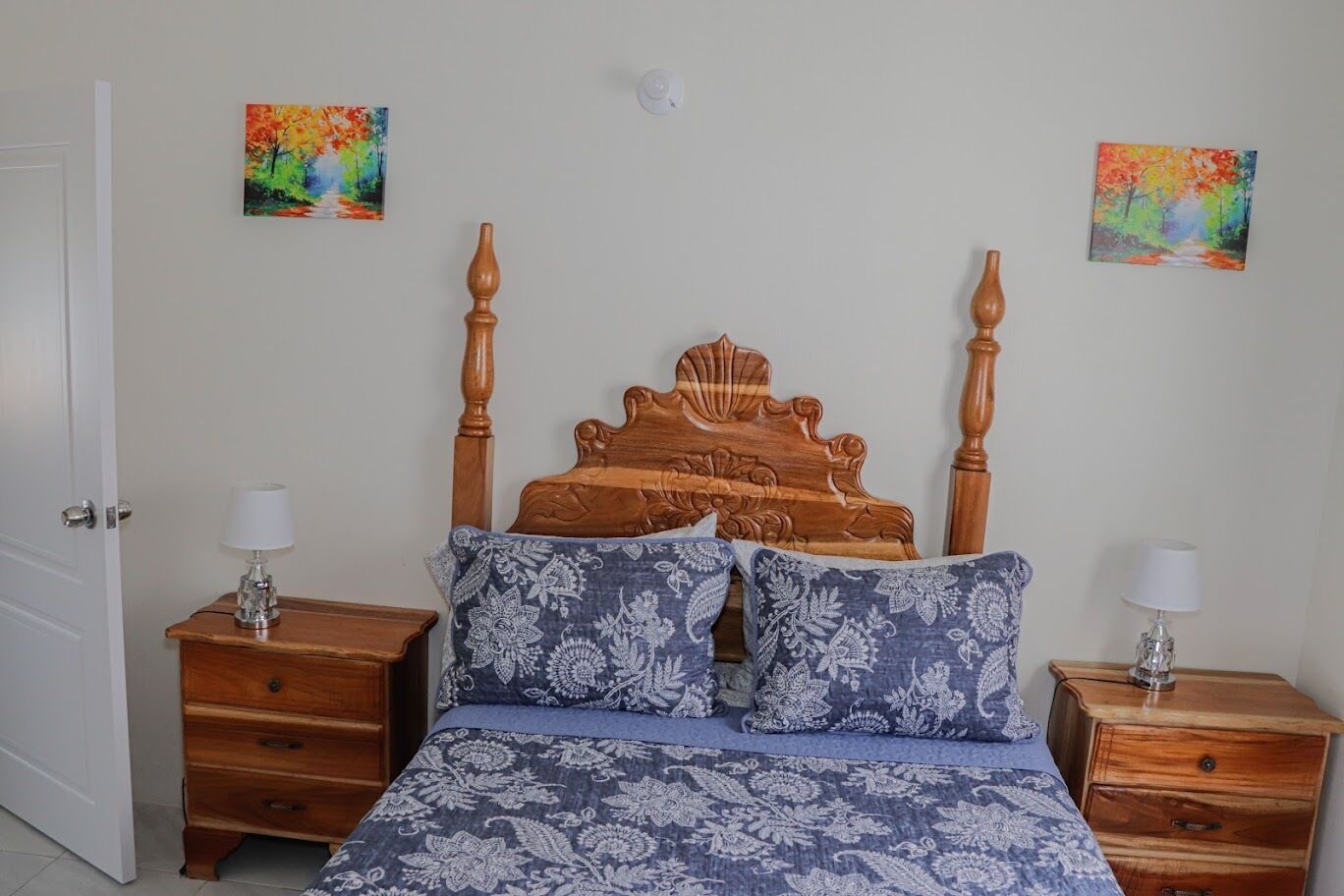 Quarto com cama de madeira, duas mesas de cabeceira e duas luminárias fixadas na parede.