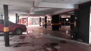 Garagem de estacionamento com chão molhado, pilares de concreto e alguns carros estacionados.