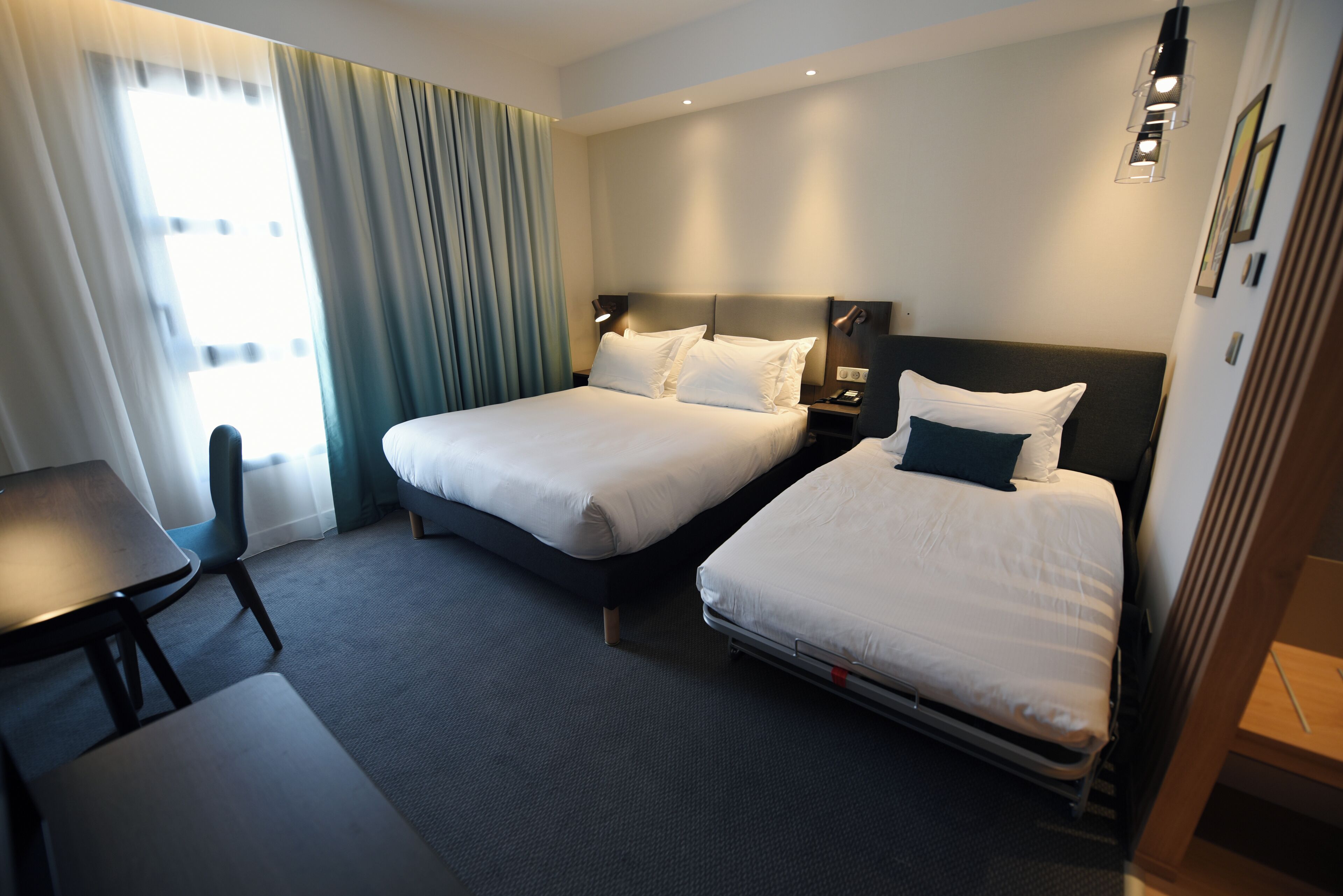 Quarto de hotel com duas camas, uma mesa e uma cadeira.