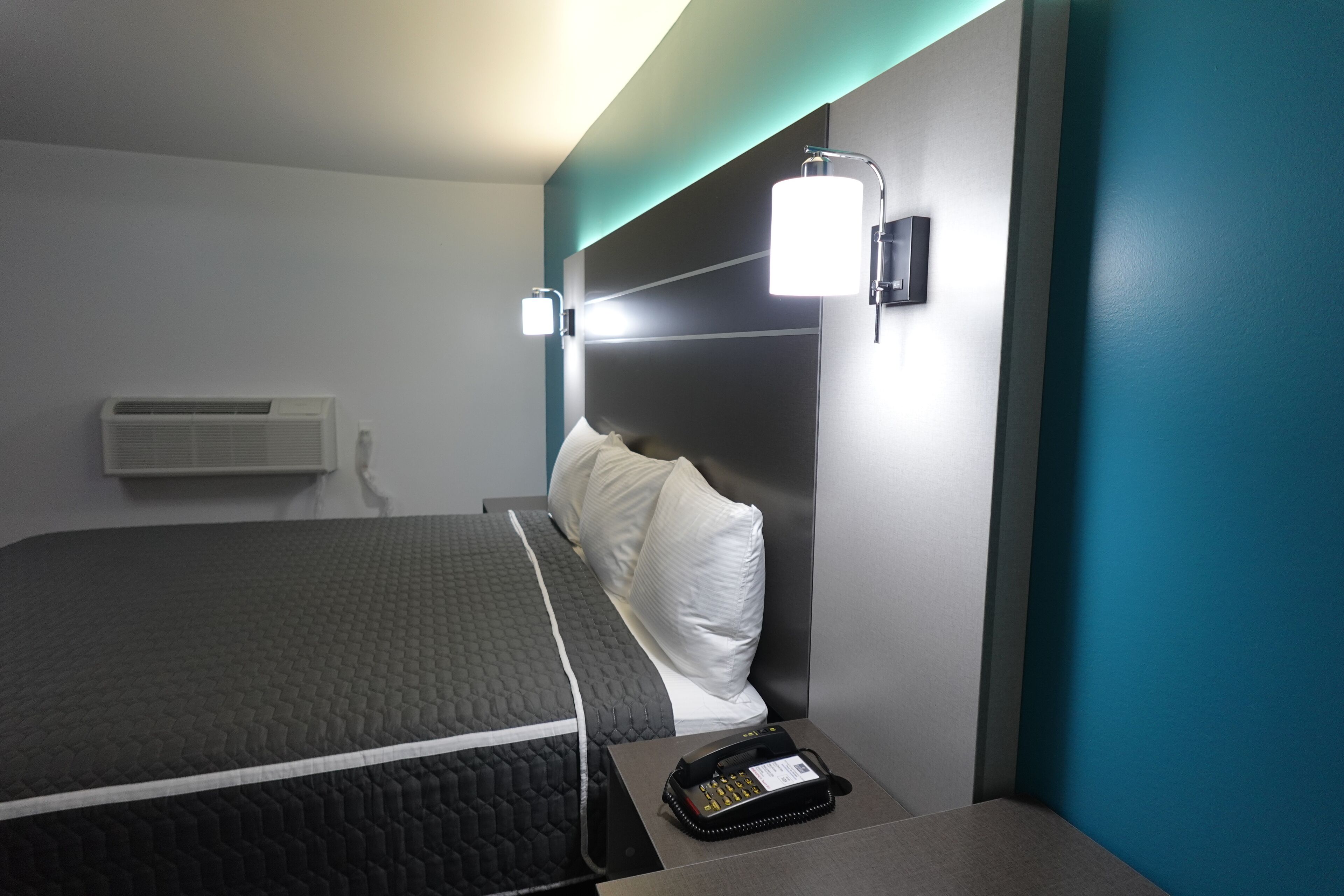Quarto de hotel com cama, mesa de cabeceira e ar condicionado fixado na parede.
