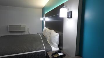 Quarto de hotel com cama, mesa de cabeceira e ar condicionado fixado na parede.