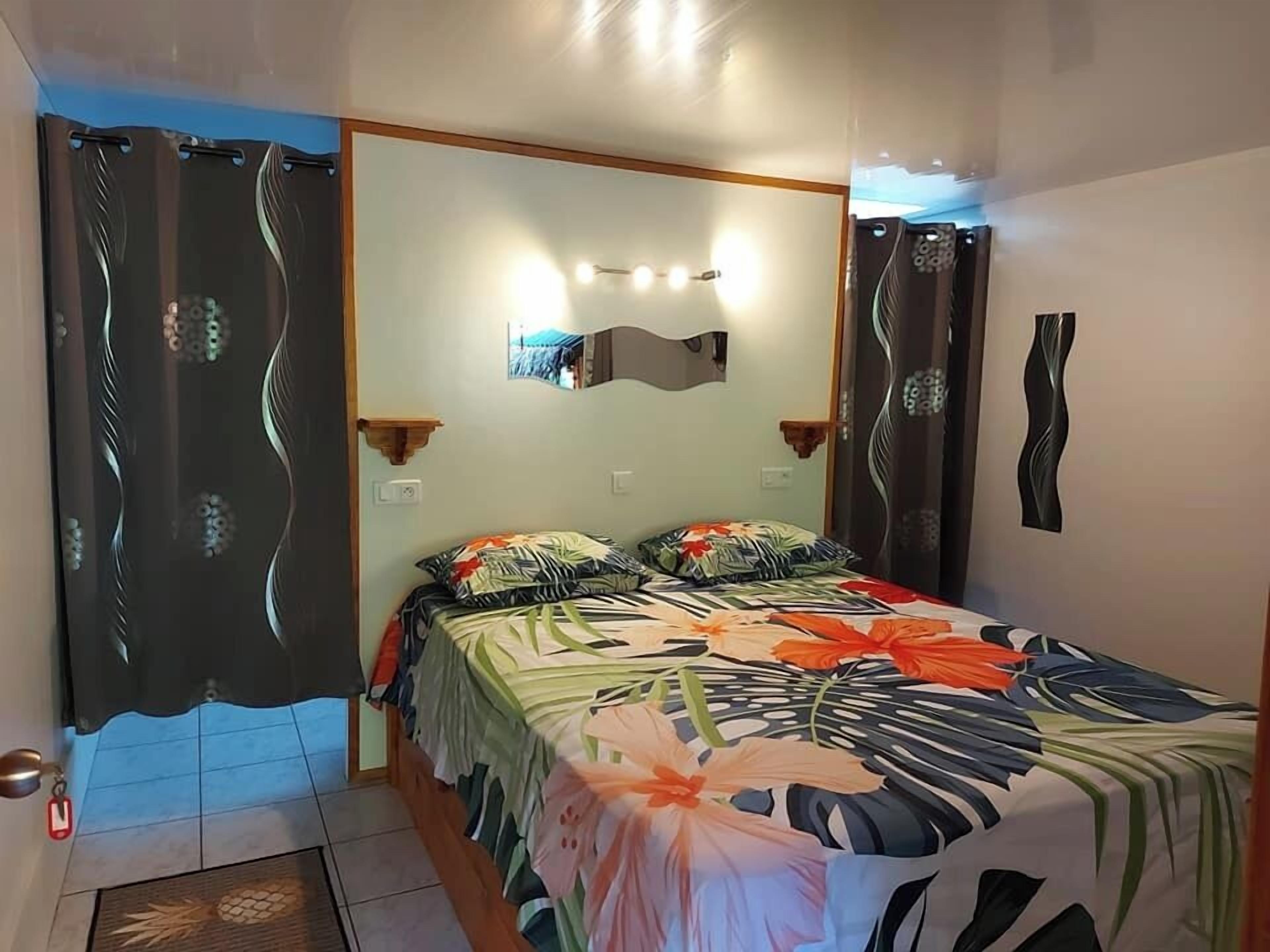 Quarto com cama, espelho e luminária fixada na parede.