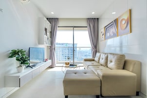 Uma sala de estar moderna com sofá, televisão, planta e vista da cidade através de amplas janelas.
