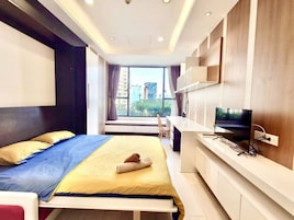 Quarto de hotel moderno com uma cama, uma escrivaninha com televisão e uma janela grande com vista para a cidade.