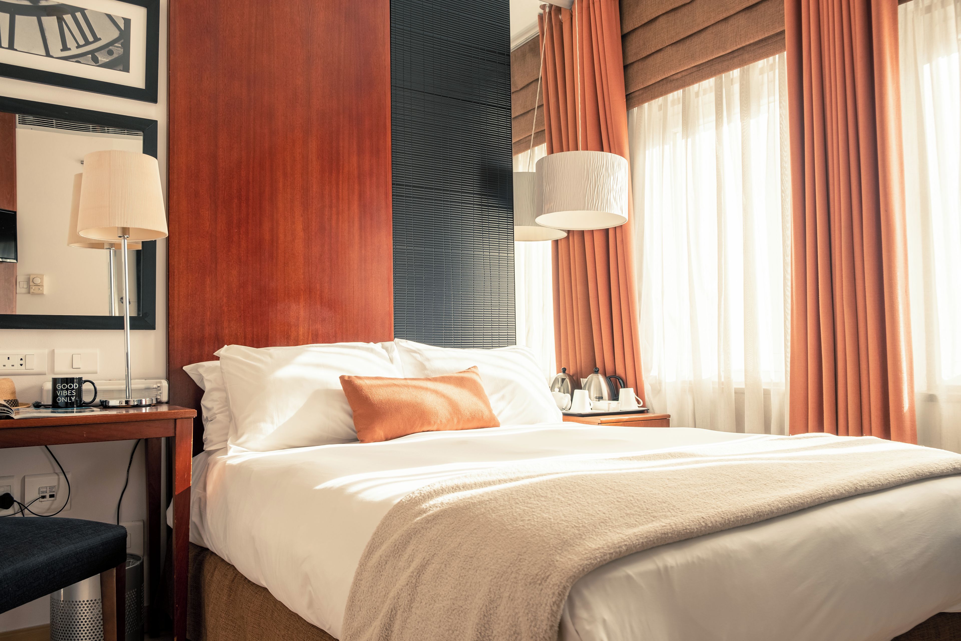 Quarto de hotel com cama, mesas de cabeceira, abajur e cortinas.