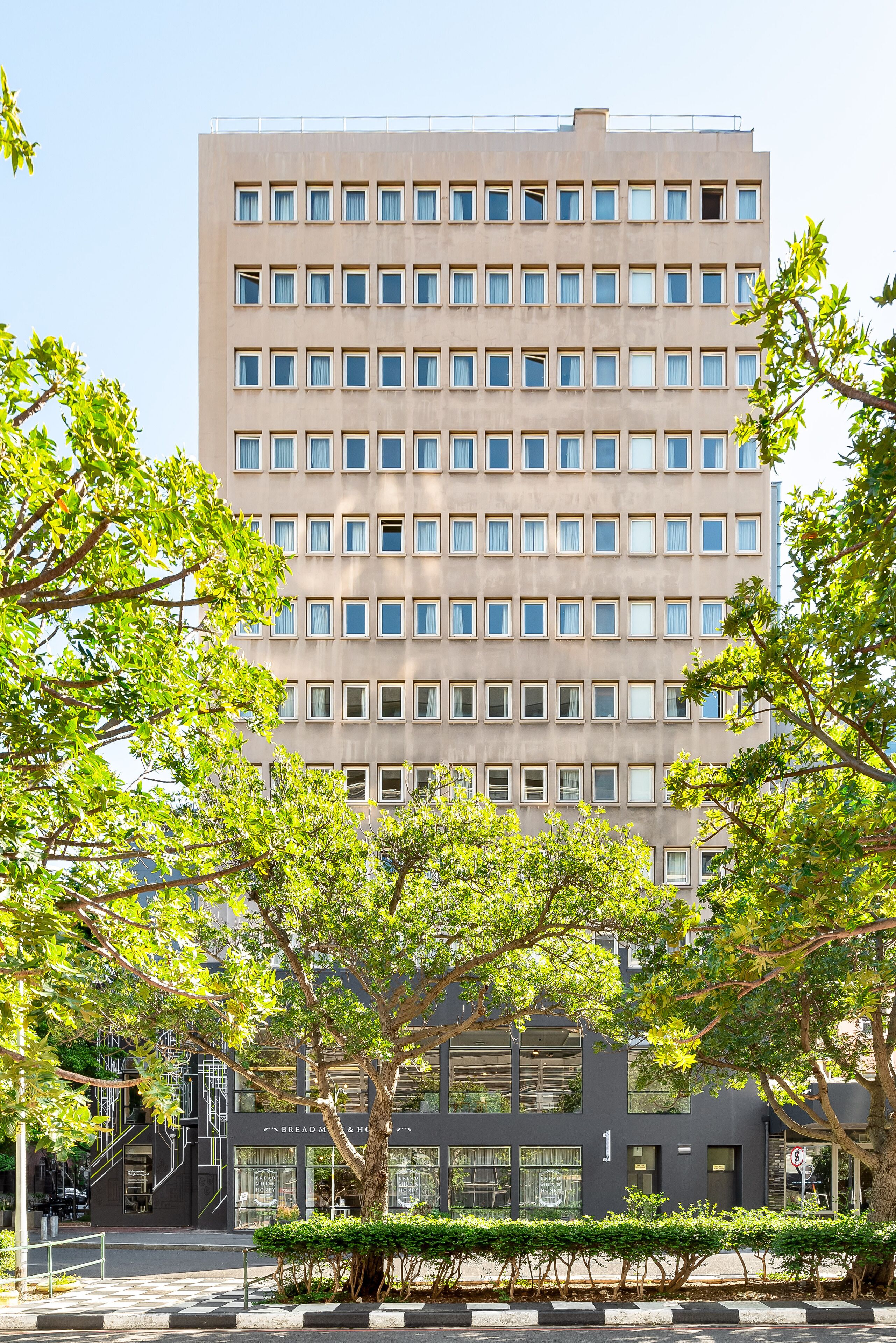 Um edifício de vários andares com fachada uniforme, várias janelas e uma entrada visível com escadaria.