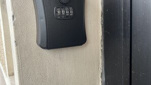 Um painel de teclado de segurança preto fixado em uma parede bege, provavelmente para uma porta ou portão.