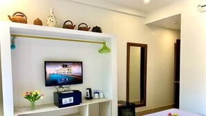 Quarto de hotel com duas camas, uma televisão numa estante, um espelho e uma estante decorada.