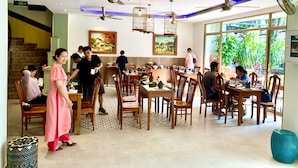 Um restaurante espaçoso com várias mesas e cadeiras, ventiladores de teto e grandes janelas que oferecem vista para o exterior.