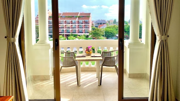 Uma varanda com mesa e cadeiras, vista para um edifício com várias varandas e vegetação.