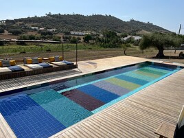 Piscina com deck de madeira e área de descanso, cercada por uma paisagem acidentada.