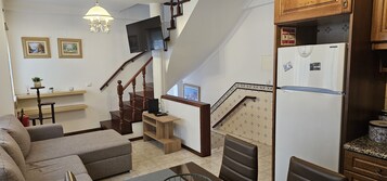 Uma sala de estar com sofá, televisão, escada e geladeira.