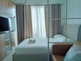 Quarto de hotel com uma cama, televisão, guarda-roupa e janela com cortinas.