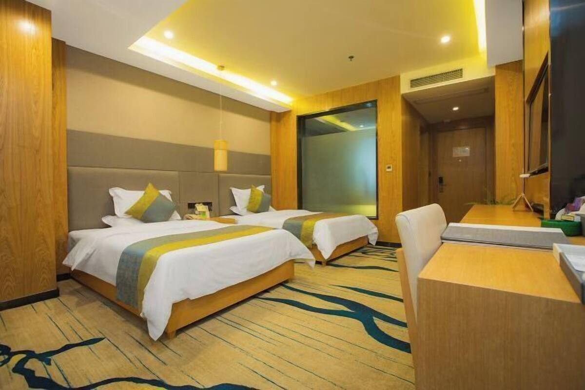 Quarto de hotel com duas camas, uma mesa de trabalho e uma janela grande.