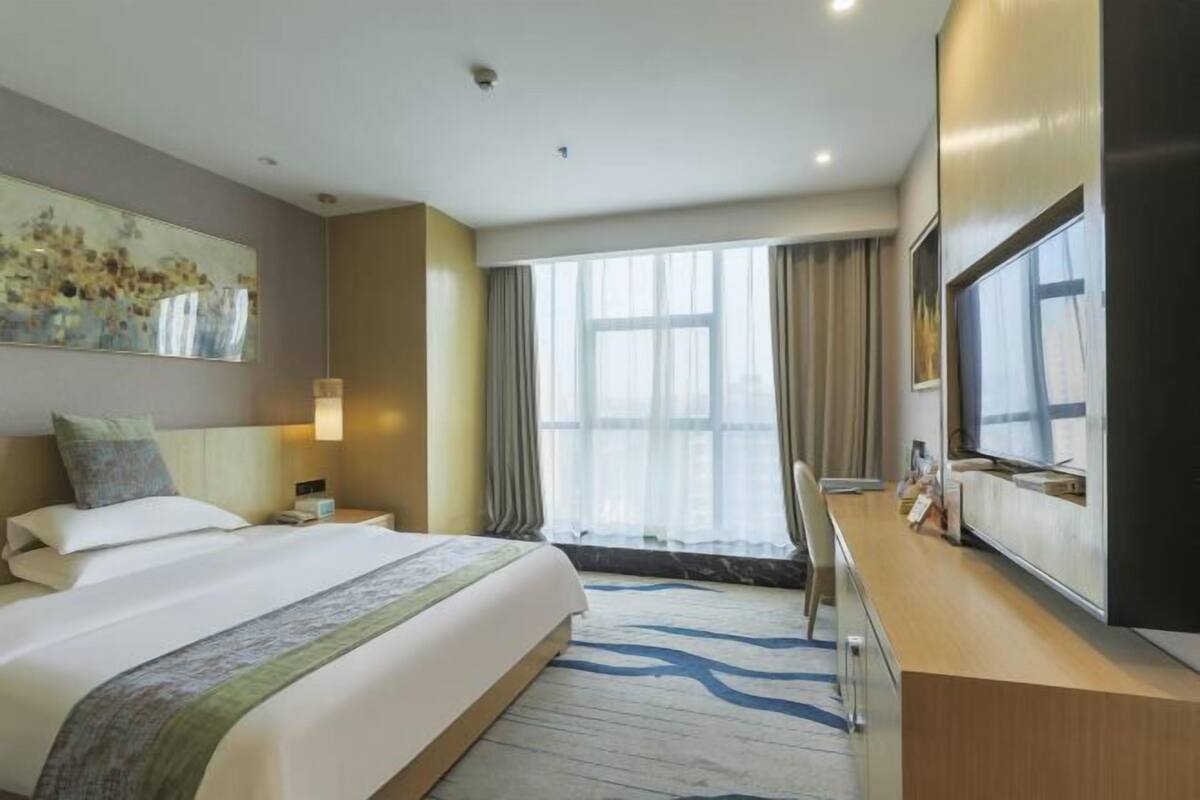 Quarto de hotel com uma cama grande, uma escrivaninha, uma televisão e uma janela com cortinas.