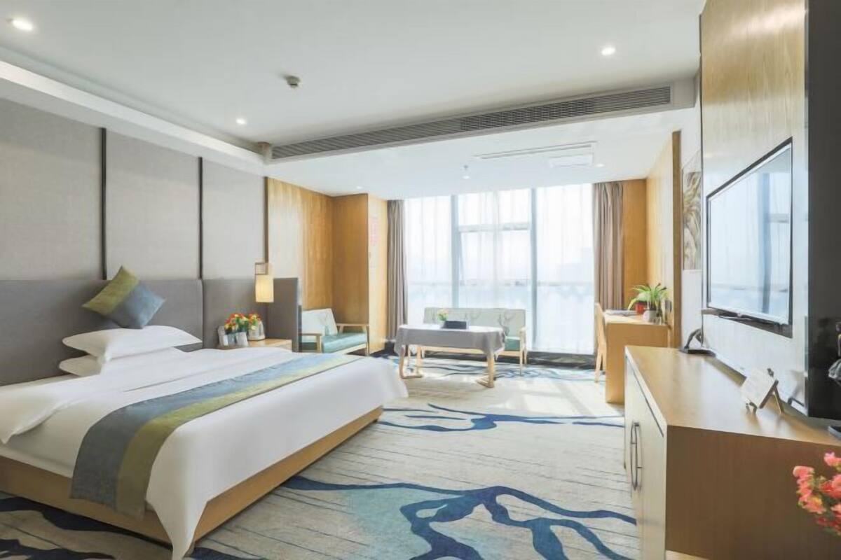 Quarto de hotel com uma cama grande, uma escrivaninha, uma cadeira e uma televisão.
