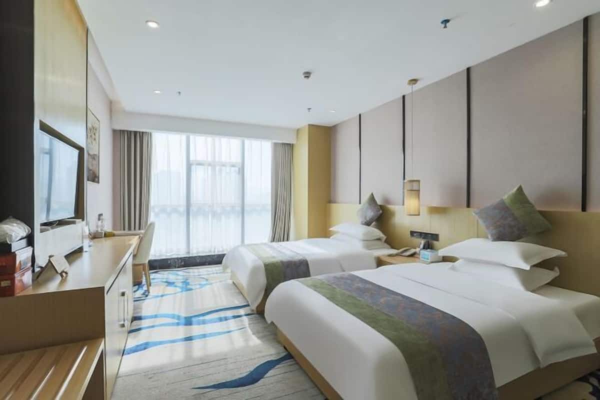 Quarto de hotel com duas camas, uma escrivaninha, televisão e uma janela grande.