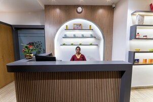 Uma receção com uma recepcionista, um relógio na parede e prateleiras com produtos ao fundo.