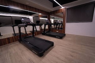 Uma academia com esteiras, piso de madeira e um espelho grande na parede.