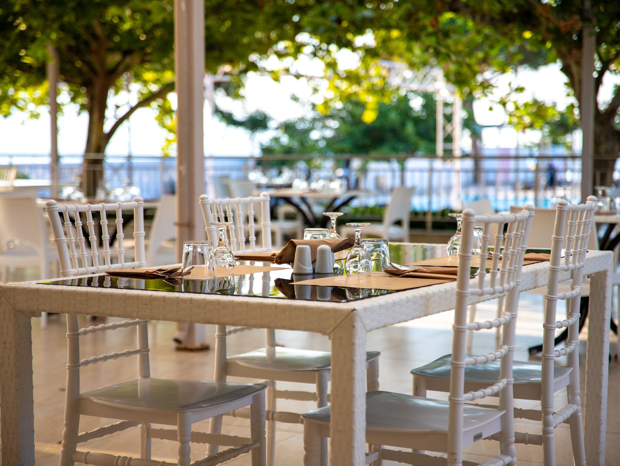 Um restaurante com cadeiras e mesas brancas, área externa e vista para o mar.