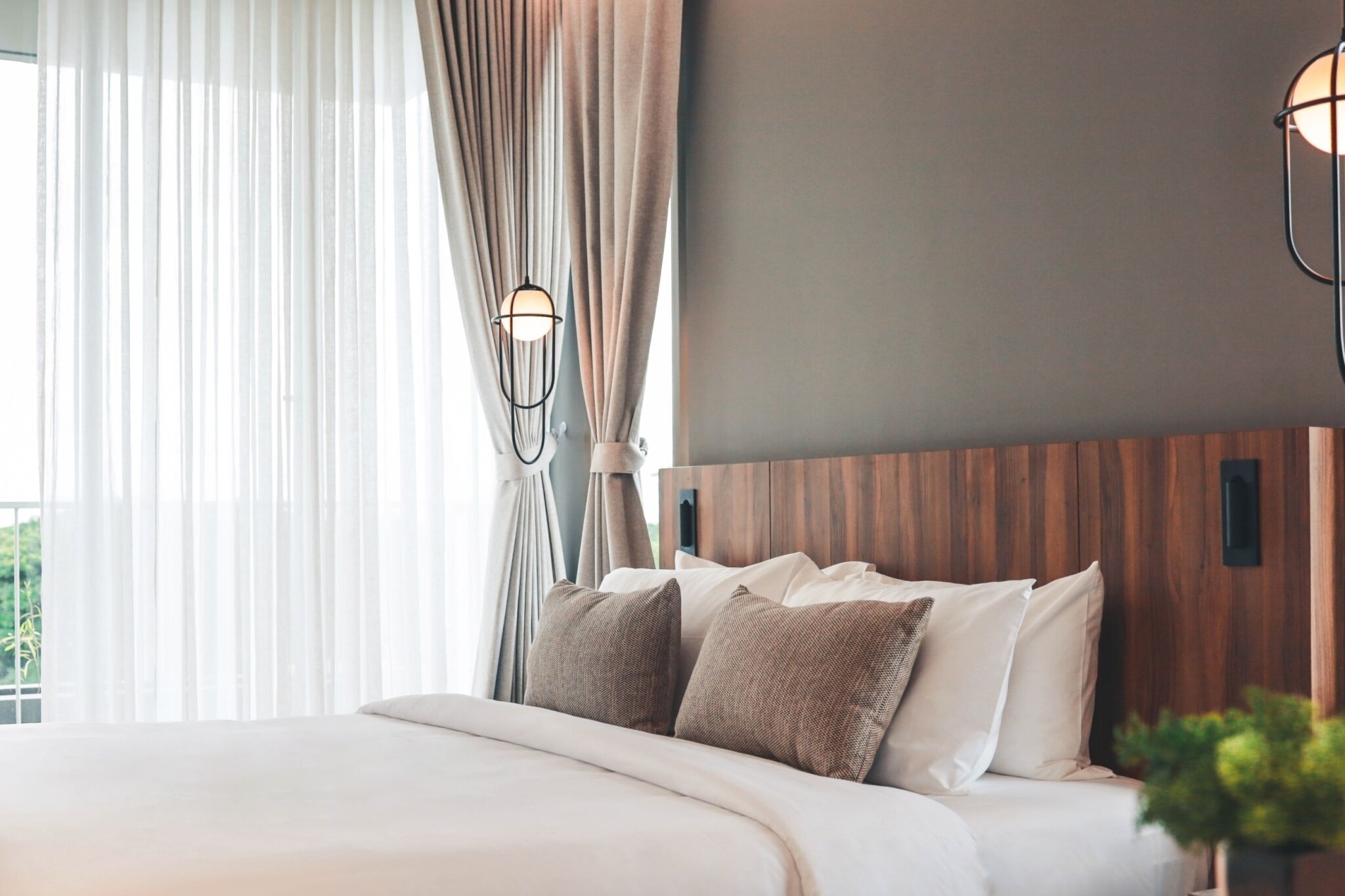 Quarto moderno com cama grande, cabeceira de madeira e duas luminárias fixadas na parede.