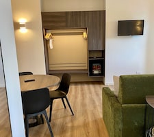 Uma sala de estar moderna com área de jantar, uma TV de tela plana na parede e um mini-refrigerador embutido.