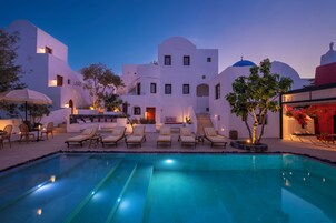 Uma área à beira da piscina com espreguiçadeiras, uma escadaria e um edifício com paredes brancas e cúpulas azuis.