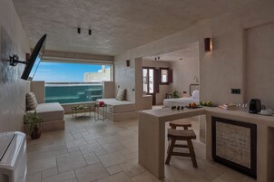 Quarto de hotel moderno com varanda, área de estar, cozinha compacta e uma cama.